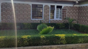 Um edifício com fachada de pedra, várias janelas e um jardim bem cuidado com sebes e uma palmeira.