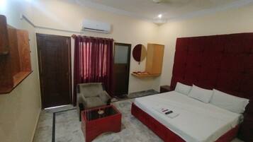 Quarto de hotel com cama, cadeira, mesa pequena, espelho e aparelho de ar condicionado.