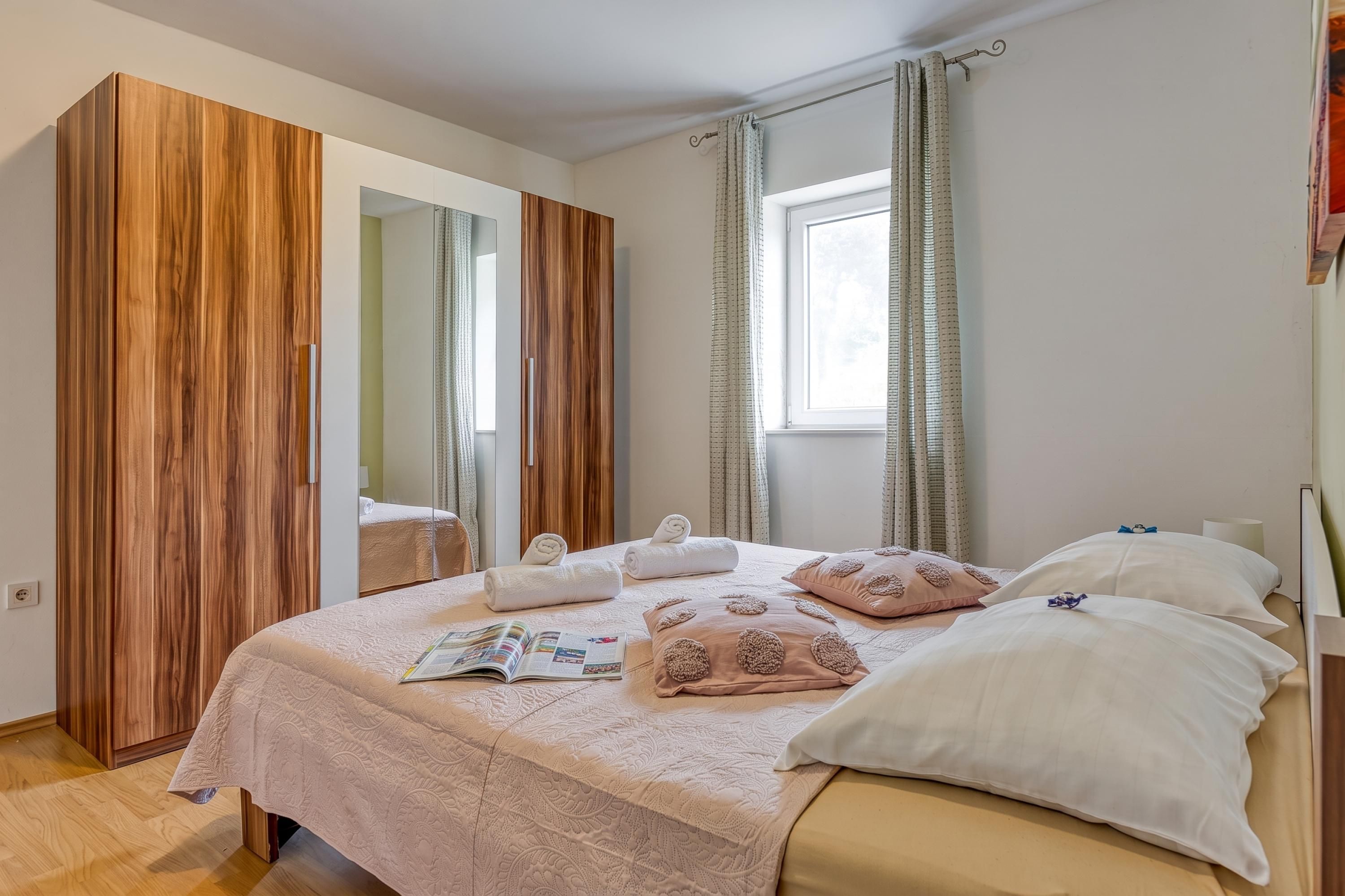 Quarto com cama, guarda-roupa de madeira, janela com cortinas e espelho.