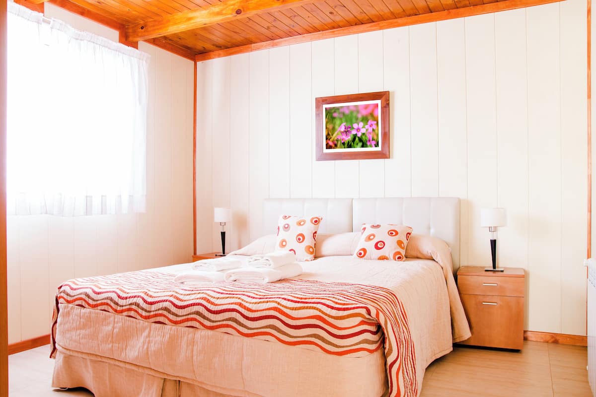 Quarto com cama, mesas de cabeceira, um quadro emoldurado e uma janela com cortinas.