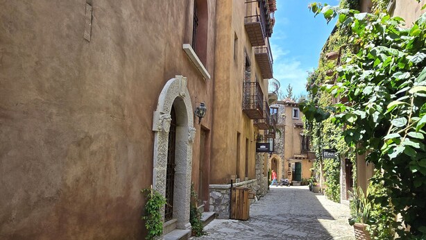 Uma rua de paralelepípedos estreita, ladeada por edifícios históricos com arcos e varandas de pedra.