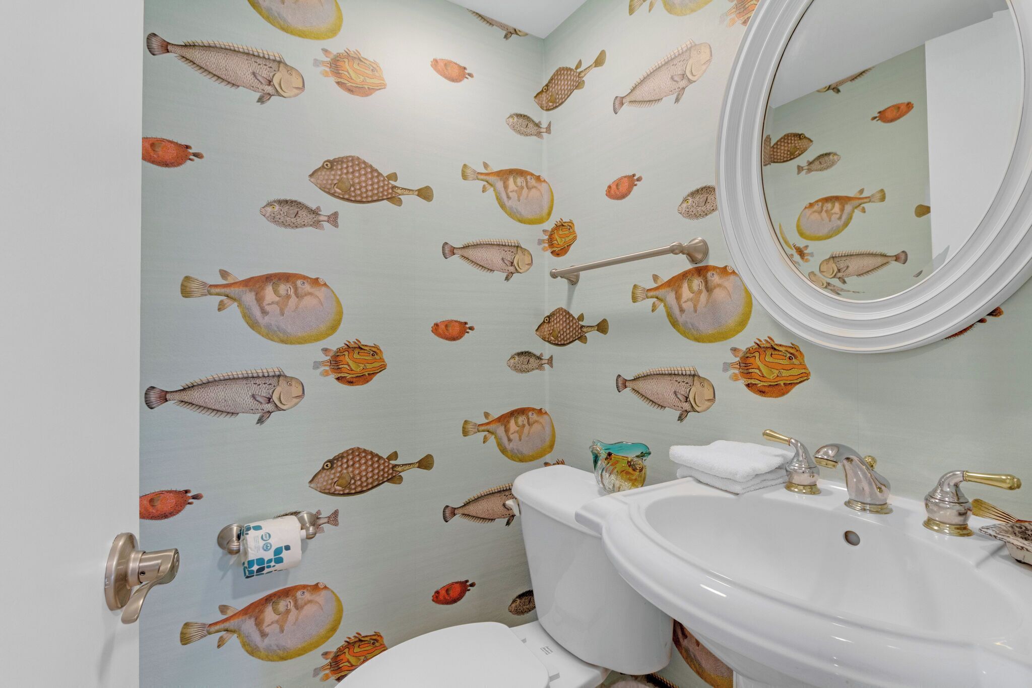 Casa de banho com sanita, lavatório e espelho. As paredes decoradas com autocolantes de peixes.