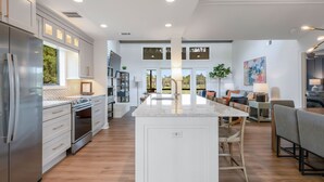Cozinha moderna com ilha central, eletrodomésticos de aço inoxidável e vista para a sala de jantar.