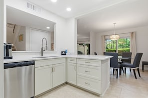 Uma cozinha moderna com armários brancos, uma lava-louças e um espaço de refeições com mesa e cadeiras.