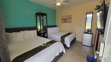Quarto de hotel com duas camas, um guarda-roupa, um ventilador de teto, um quadro e um minibar.