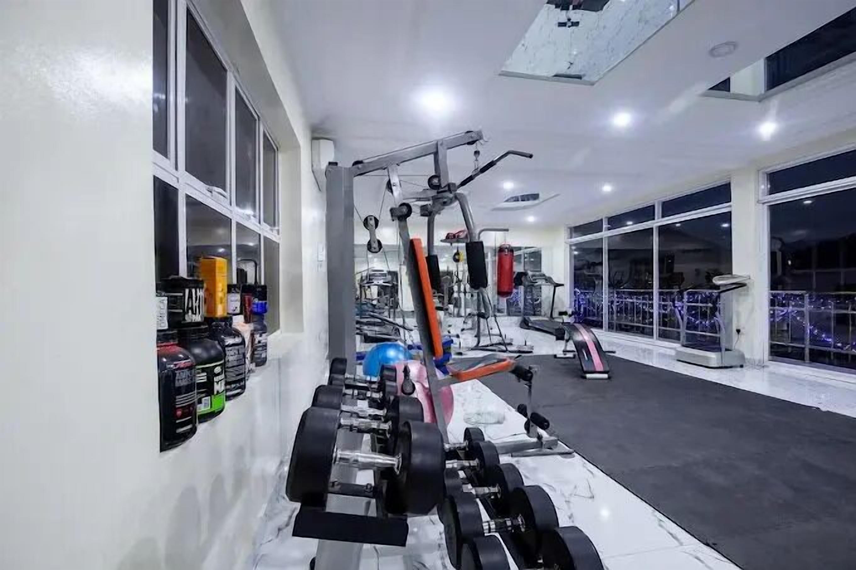 Academia com diversos equipamentos de exercício, incluindo halteres, supino e barra fixa.