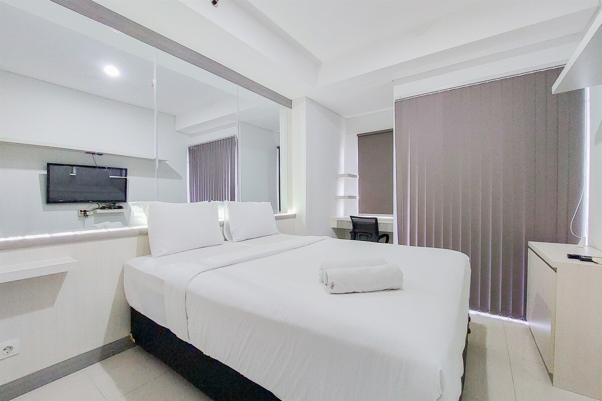 Quarto de hotel com uma cama grande, uma escrivaninha, uma cadeira, televisão e um espelho.