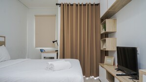 Quarto de hotel com cama, escrivaninha, televisão e cortina.