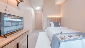 Quarto de hotel com cama, mesa de cabeceira e televisão de tela plana exibindo a interface de um serviço de streaming.