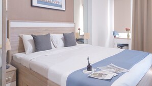 Cama bem arrumada com colcha azul, quadro na parede e escrivaninha com luminária e flores.