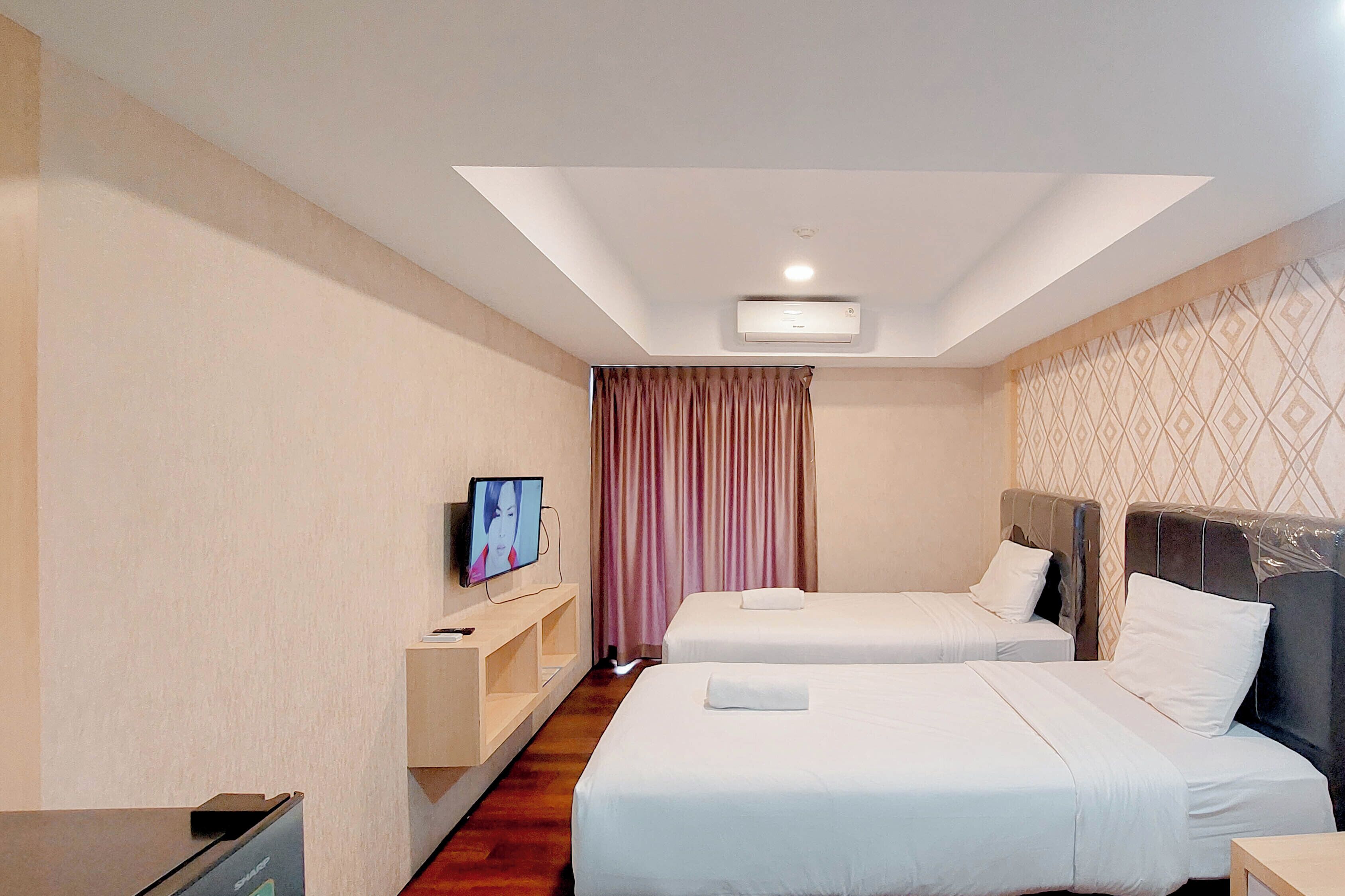 Quarto de hotel com duas camas, televisão, secretária e uma lâmpada no teto.