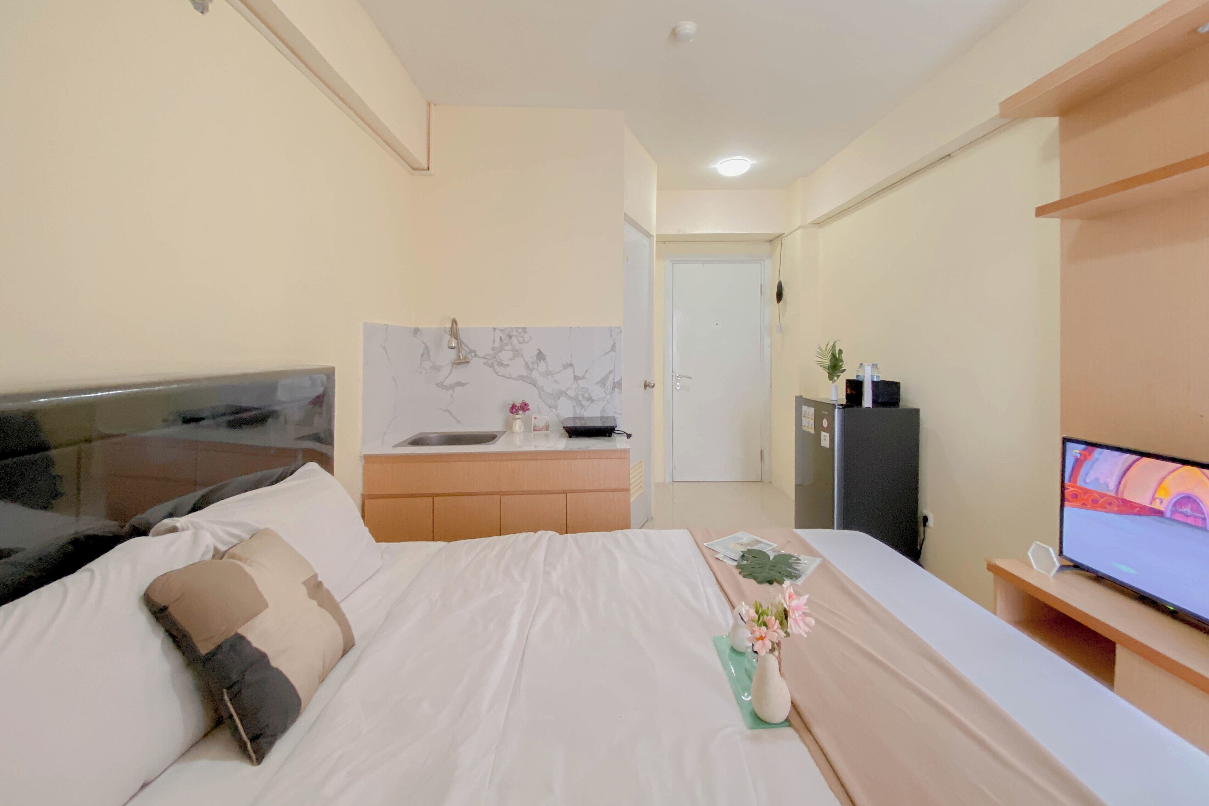 Quarto de hotel com cama, televisão, uma pequena kitchenette e banheiro.