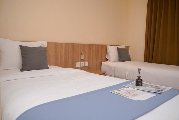 Quarto de hotel com duas camas, uma cabeceira de madeira, mesa de cabeceira e uma pequena mesa com uma vela e uma revista.