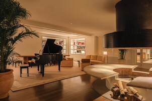 Uma sala de estar espaçosa com um piano de cauda, um sofá confortável, uma mesa de centro e uma estante repleta de livros.