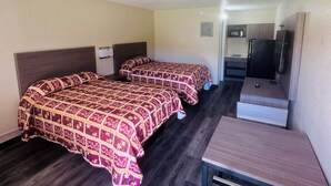 Quarto de hotel com duas camas, uma escrivaninha, uma cadeira, uma televisão e uma cozinha compacta.