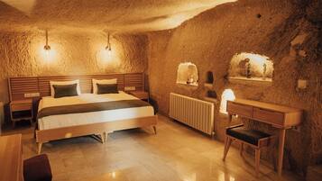 Quarto com cama grande, cabeceira de madeira, mesas de cabeceira, escrivaninha e uma cadeira.