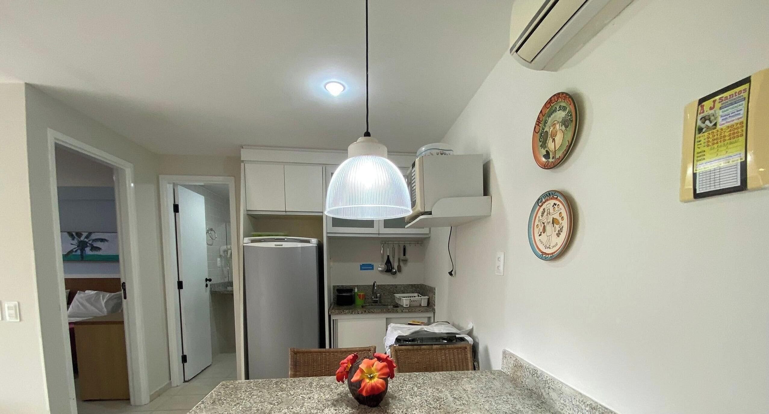 Uma cozinha com geladeira, luminária pendente e ar-condicionado fixado na parede.