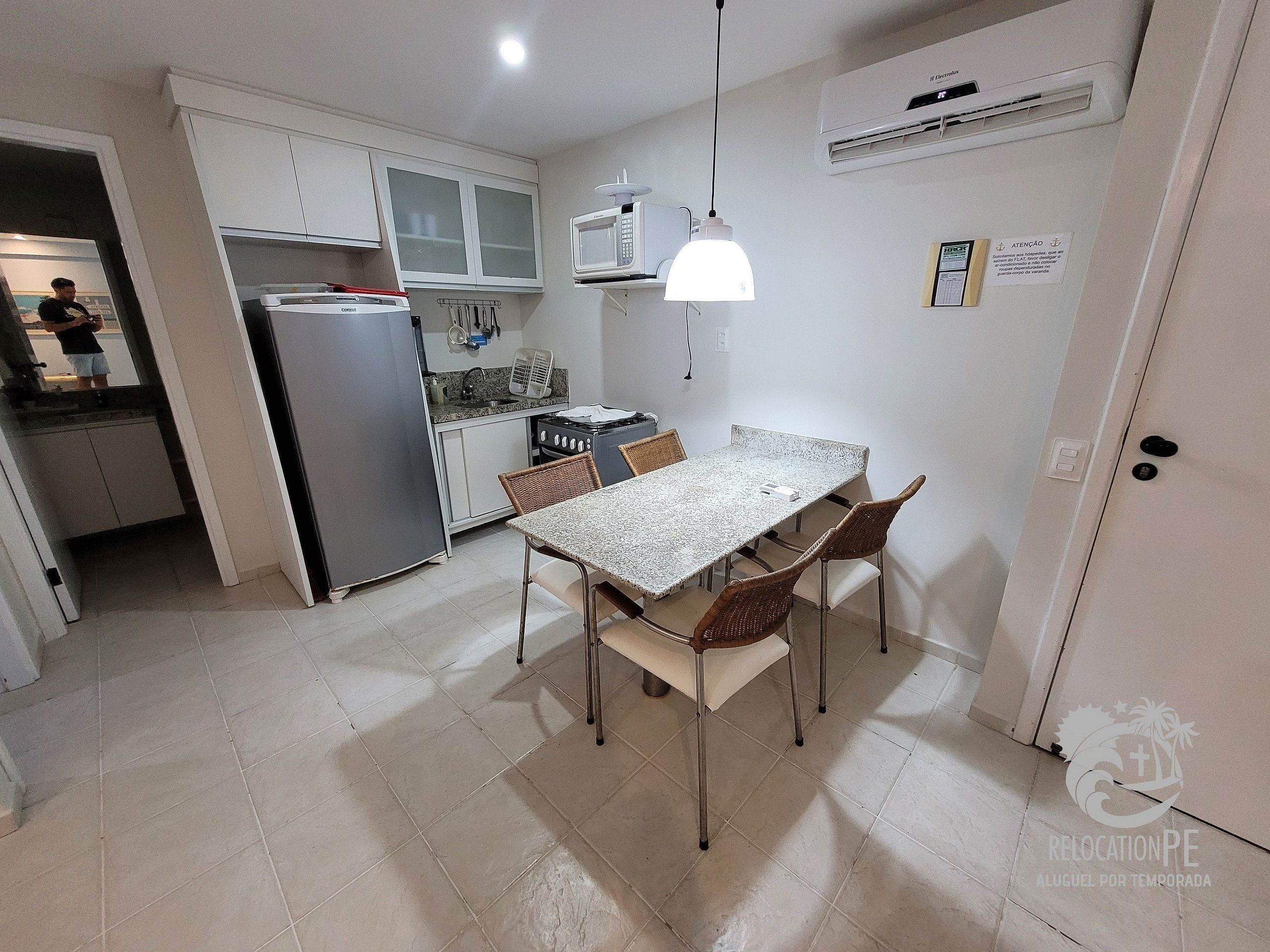 Cozinha compacta com geladeira, micro-ondas e fogão. Há uma mesa de jantar com cadeiras e um lustre.