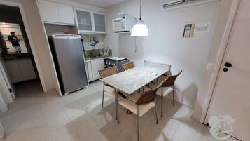 Cozinha compacta com geladeira, micro-ondas e fogão. Há uma mesa de jantar com cadeiras e um lustre.
