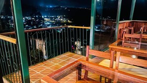 Varanda com móveis de madeira e vista para uma cidade à noite.