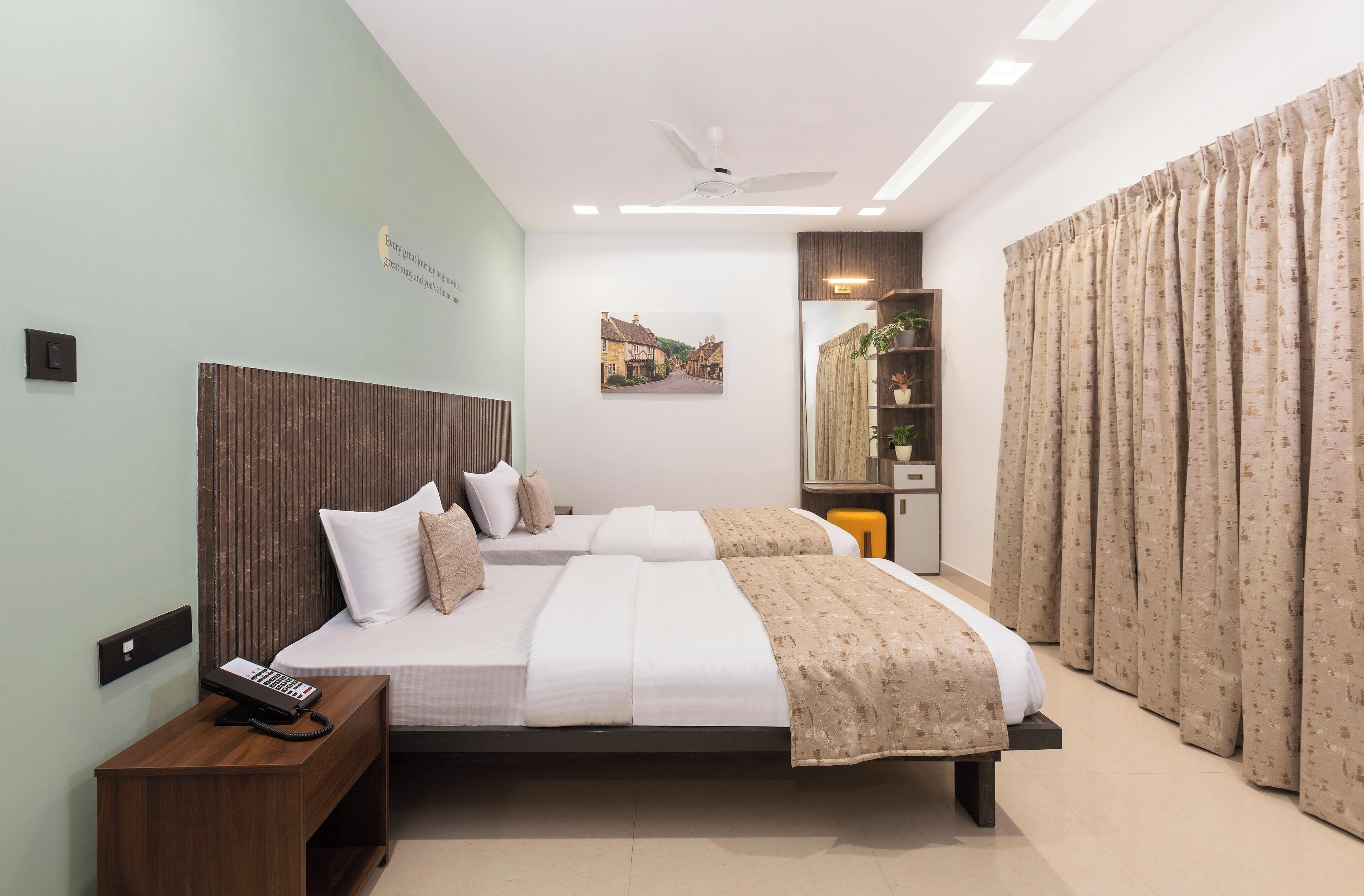 Quarto de hotel moderno com uma cama grande, mesas de cabeceira, ventilador de teto e vista para a rua pela janela.