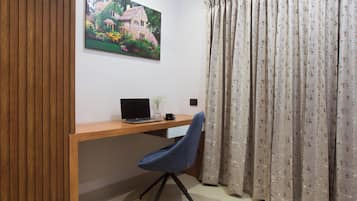 Um quarto com escrivaninha de madeira, um laptop, uma cadeira, um quadro e uma cortina.