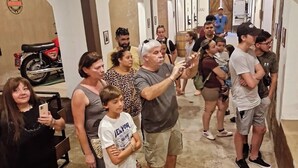 Um grupo de pessoas em um corredor com portas em arco e uma motocicleta ao fundo.