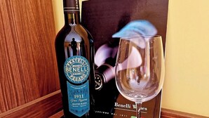 Uma garrafa de vinho Benelli, uma taça de vinho e um saca-rolhas sobre uma bandeja com tecido verde.