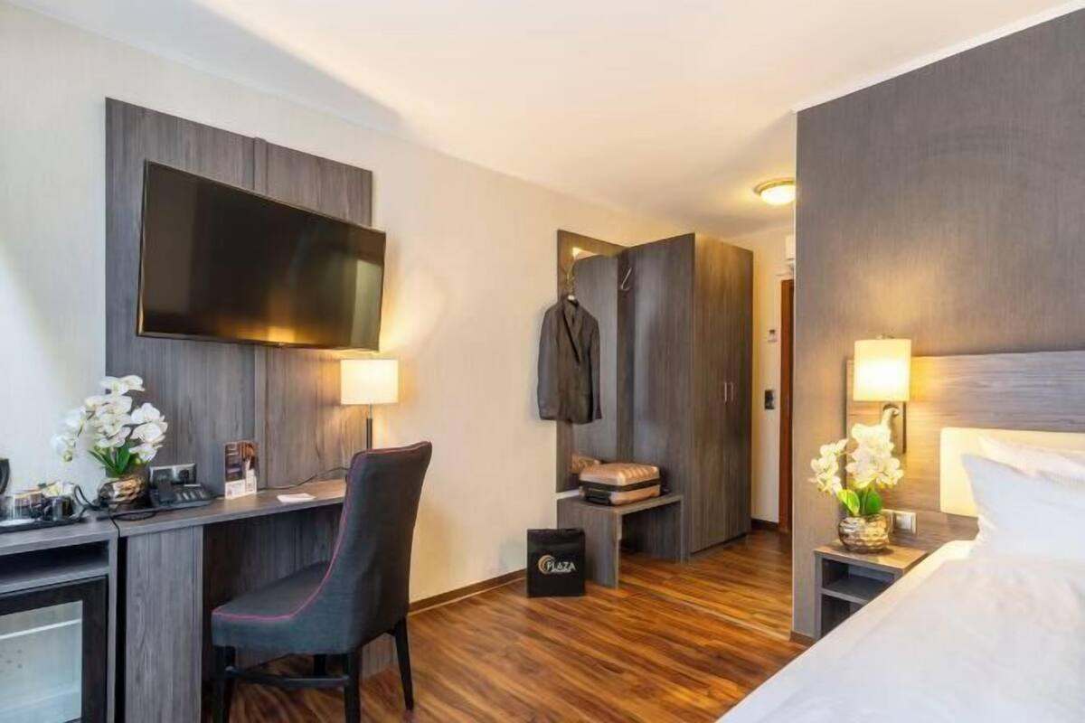 Quarto de hotel com escrivaninha, cadeira, cama, televisão e armário.