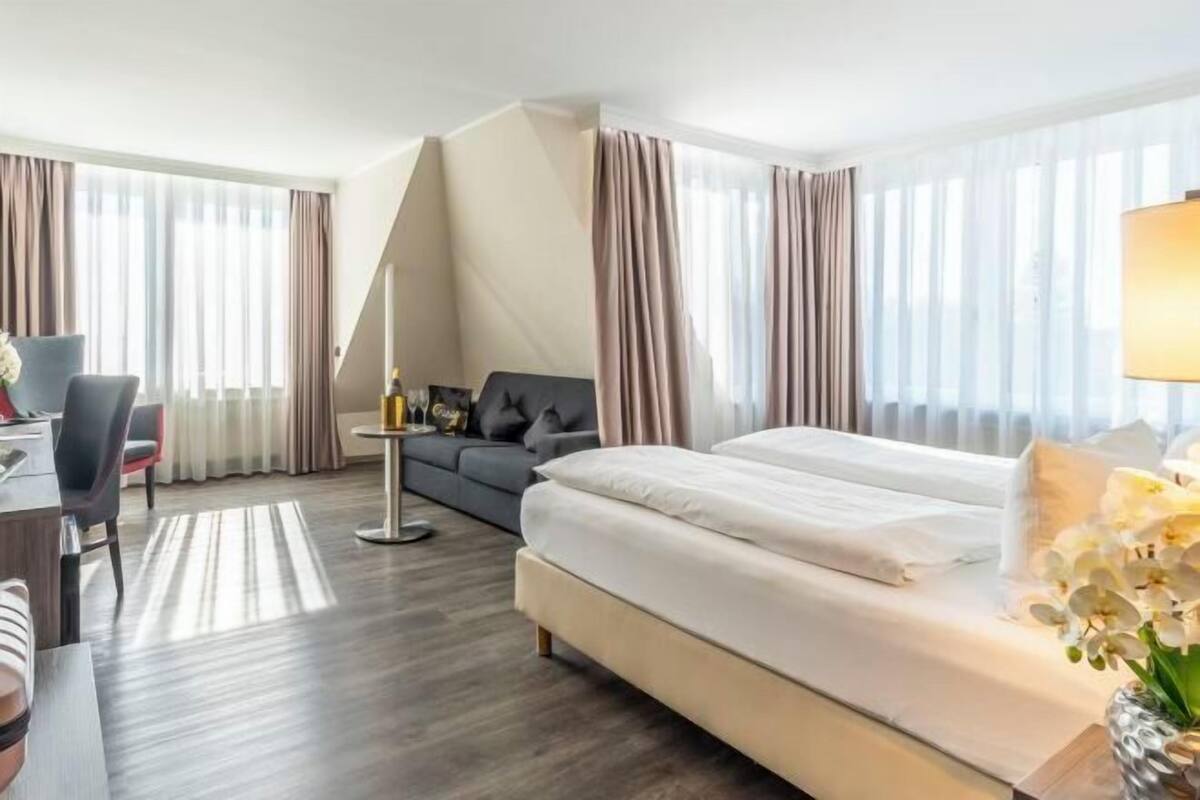 Quarto de hotel com uma cama grande, uma escrivaninha, um sofá e uma luminária.