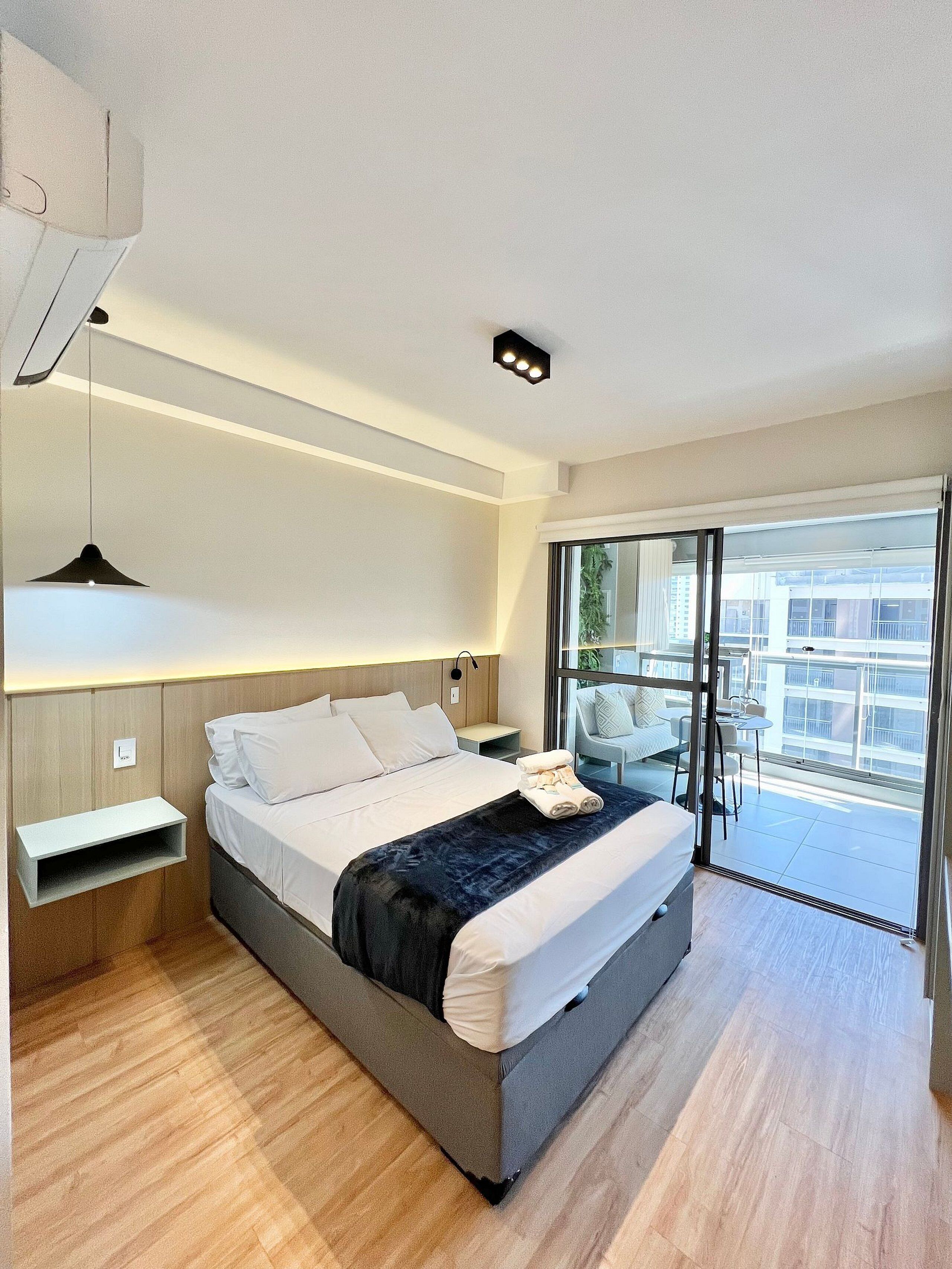 Quarto de hotel moderno com cama grande, mesas de cabeceira, escrivaninha e varanda com vista.