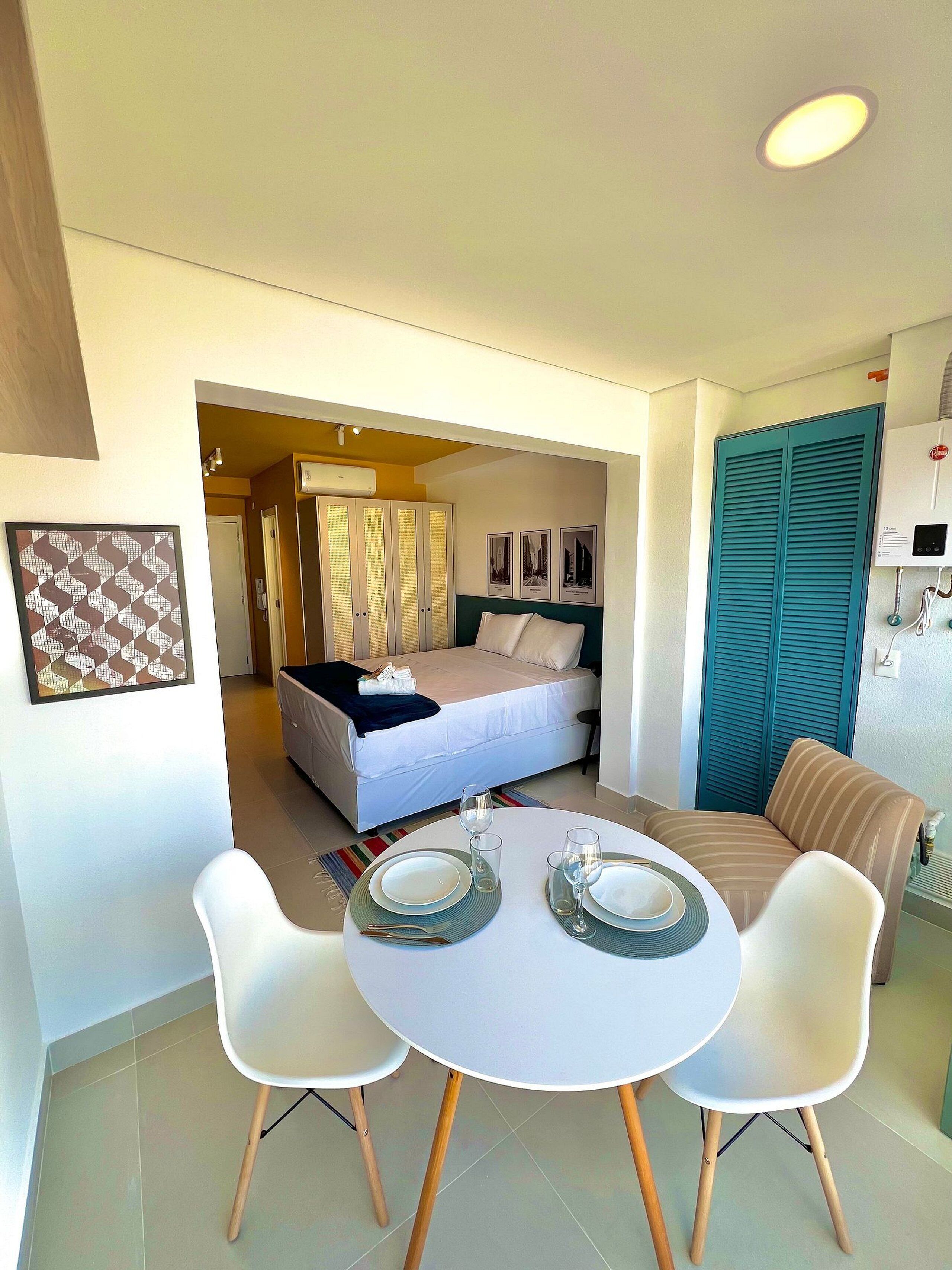 Quarto de hotel moderno com uma cama, uma mesa de jantar com cadeiras, um sofá e uma cozinha compacta.