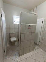 Um banheiro pequeno revestido com azulejos, com vaso sanitário, chuveiro e janela.