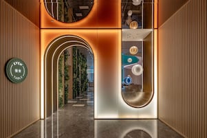 Interior moderno com balcão de recepção, parede curva com superfície refletora e corredor que leva a outra área.
