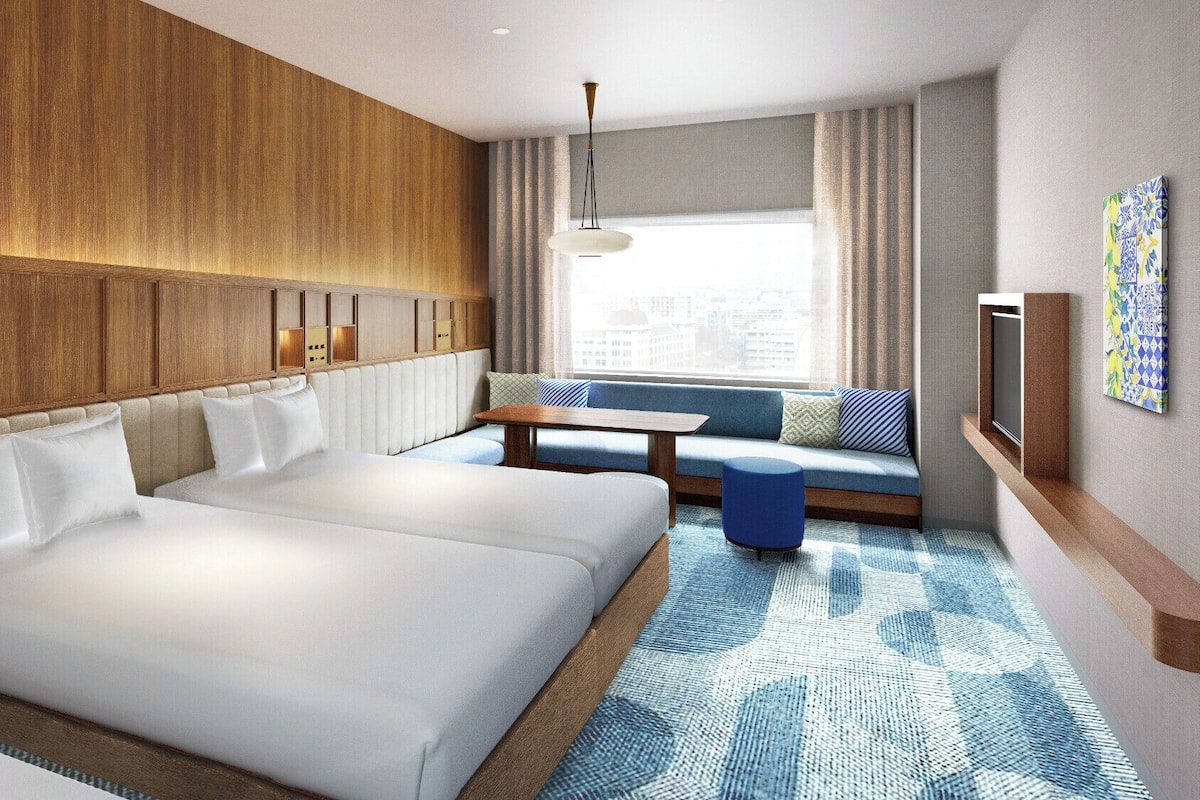 Quarto de hotel com uma cama grande, área de estar, televisão e vista para a cidade.