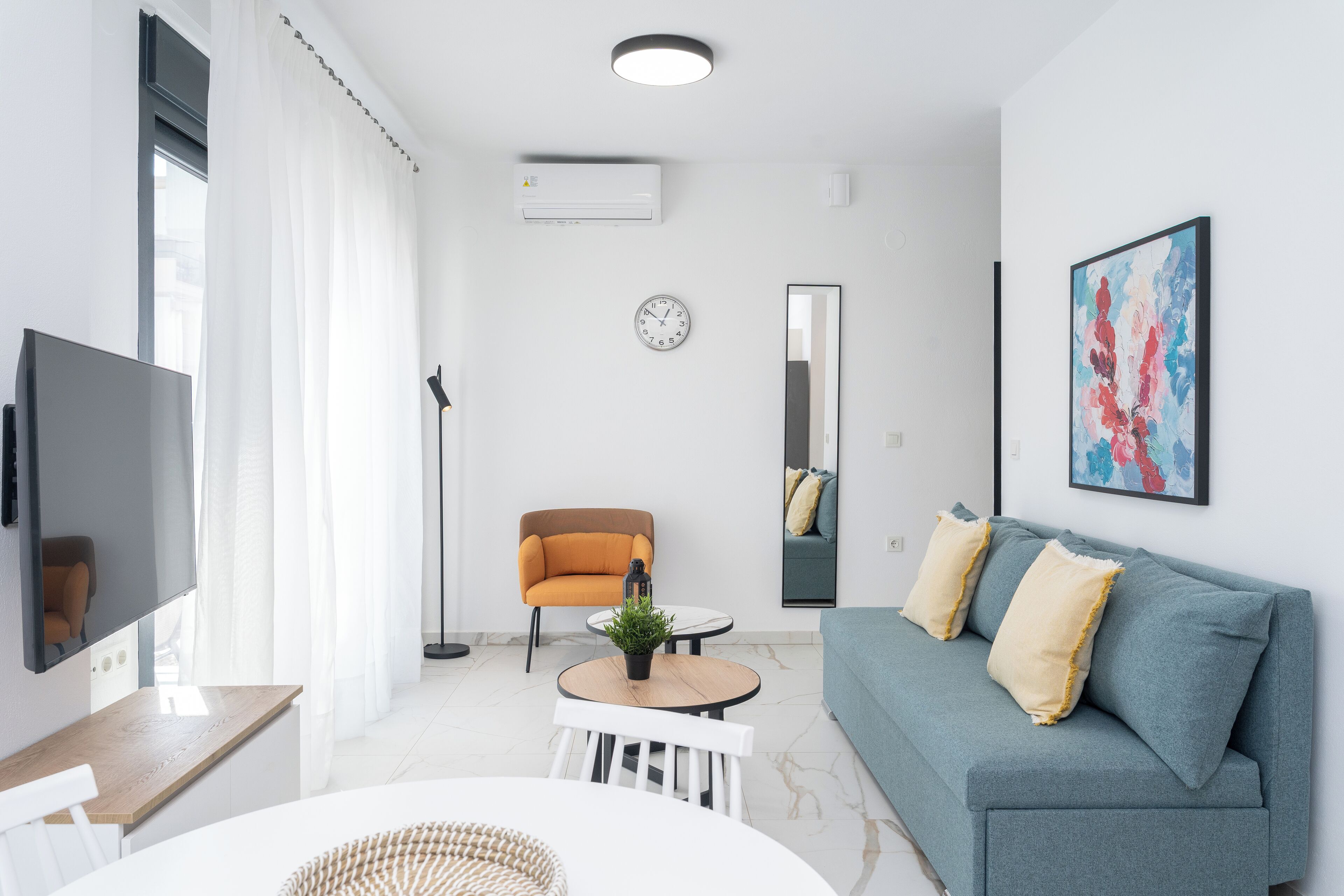 Uma sala de estar moderna com uma televisão de tela plana, um sofá, uma mesa de centro e uma poltrona.