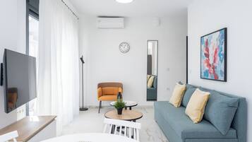Uma sala de estar moderna com uma televisão de tela plana, um sofá, uma mesa de centro e uma poltrona.