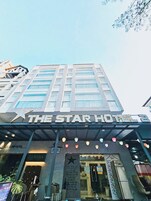 Um hotel com um logotipo de estrela bem visível, vários andares e uma área de varanda com luzes penduradas.