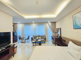 Quarto de hotel com uma cama, televisão, sofá, mesinha e secretária.