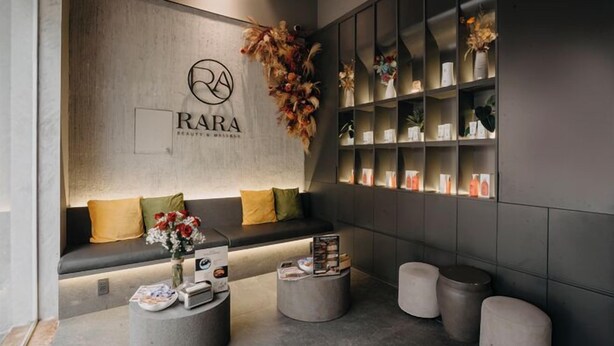 Uma área de recepção moderna com um sofá, uma mesa de centro e uma estante com diversos objetos.
