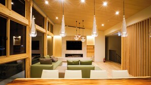 Uma sala de estar moderna com mesa de jantar de madeira, sofás verdes e luminárias pendentes.