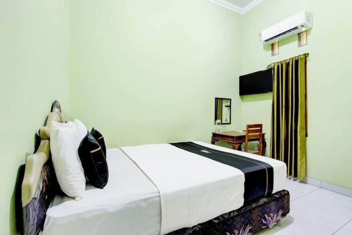 Quarto com cama, escrivaninha, cadeira, televisão e ar condicionado.