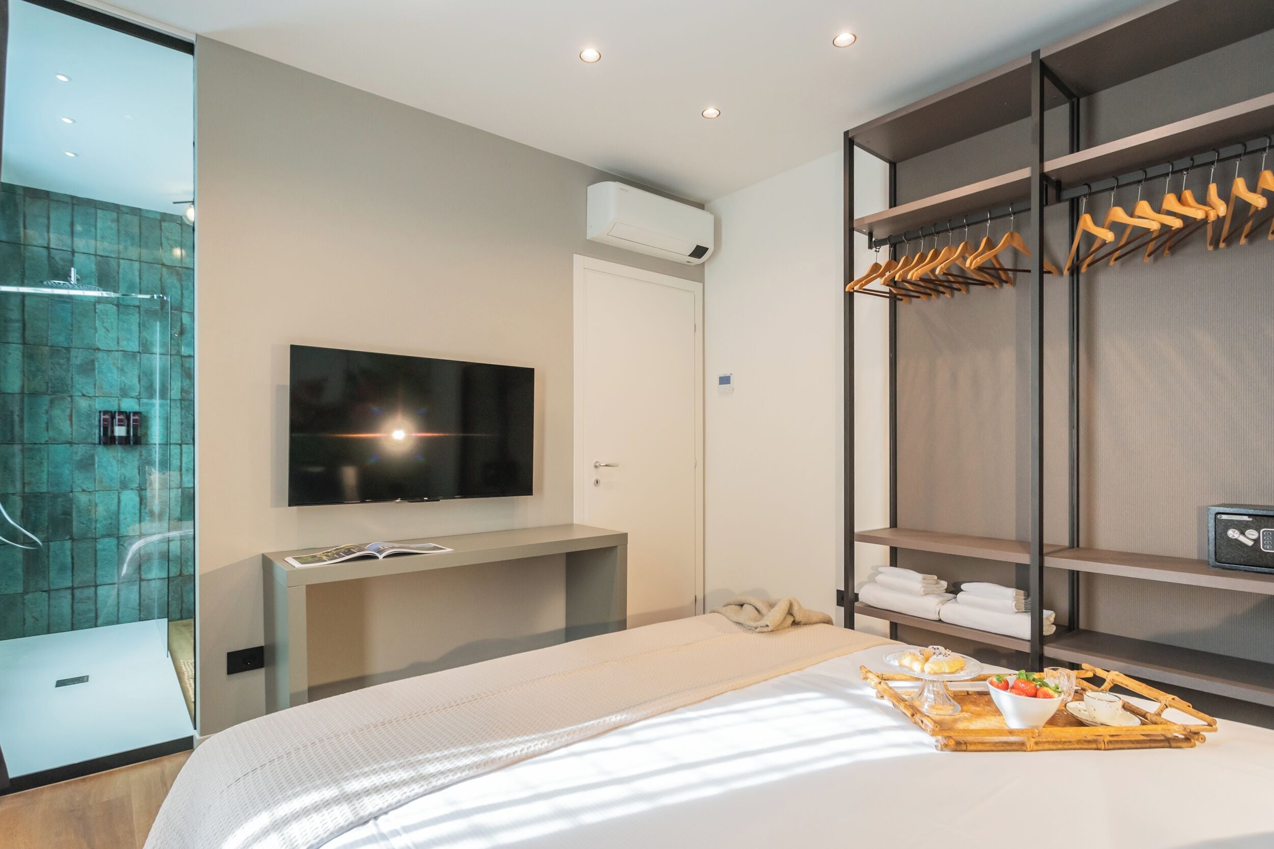 Quarto de hotel moderno com cama, televisão, escrivaninha e guarda-roupa com roupas penduradas.