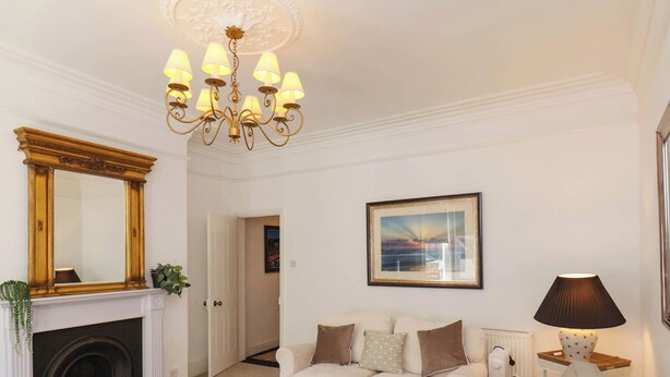 Uma sala de estar com lareira, um sofá branco, um candelabro e um quadro na parede.