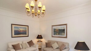 Uma sala de estar com dois sofás, uma mesa de centro de vidro, um candelabro e duas quadros nas paredes.