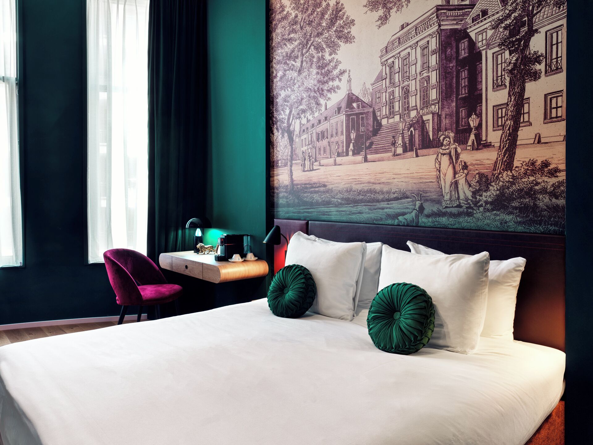 Quarto de hotel com cama, escrivaninha, cadeira e um grande mural na parede.