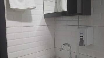 Casa de banho com paredes revestidas a azulejos brancos, uma pia branca, um espelho e um porta-toalhas com duas toalhas.