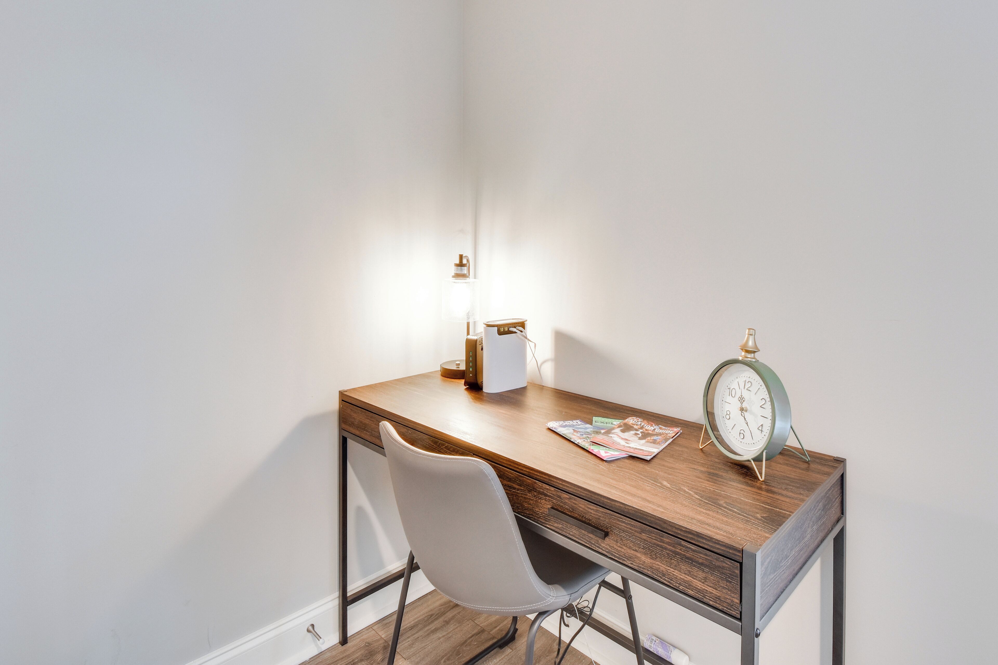 Uma pequena mesa com uma lâmpada, um relógio e uma cadeira num canto do quarto.