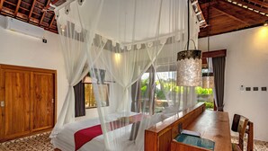 Quarto com cama sob mosquiteiro, escrivaninha de madeira e vista para o verde lá fora.