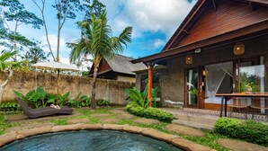 Uma piscina com espreguiçadeira, um prédio de madeira com grandes janelas e vegetação exuberante.
